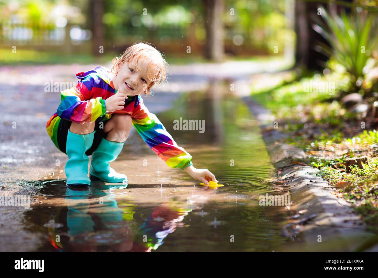 Kid playing in the rain in autumn park. Child jumping in muddy puddle ...