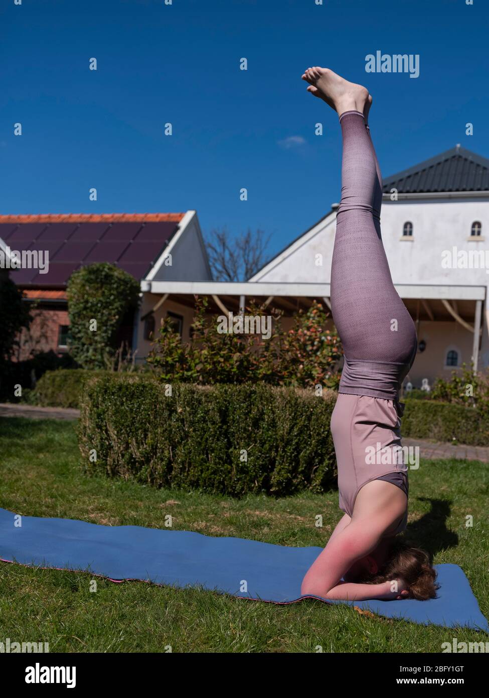 Young woman doing yoga exercises in the garden at home. headstand pose ...