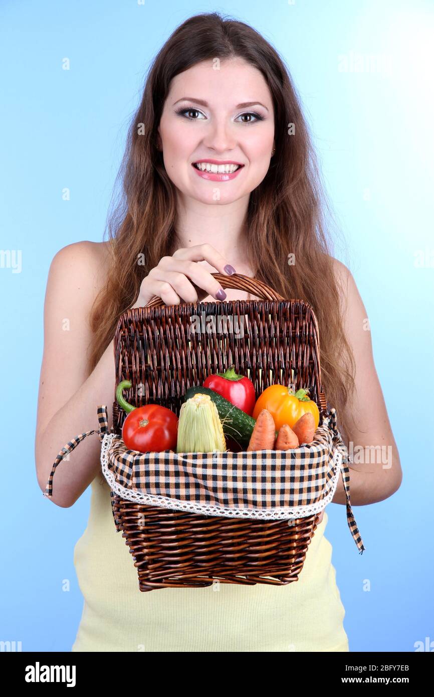 Beautiful woman with vegetables in wicker basket on blue background ...