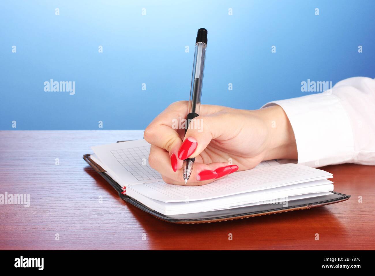 Hand signing in notebook on wooden table on color background Stock ...