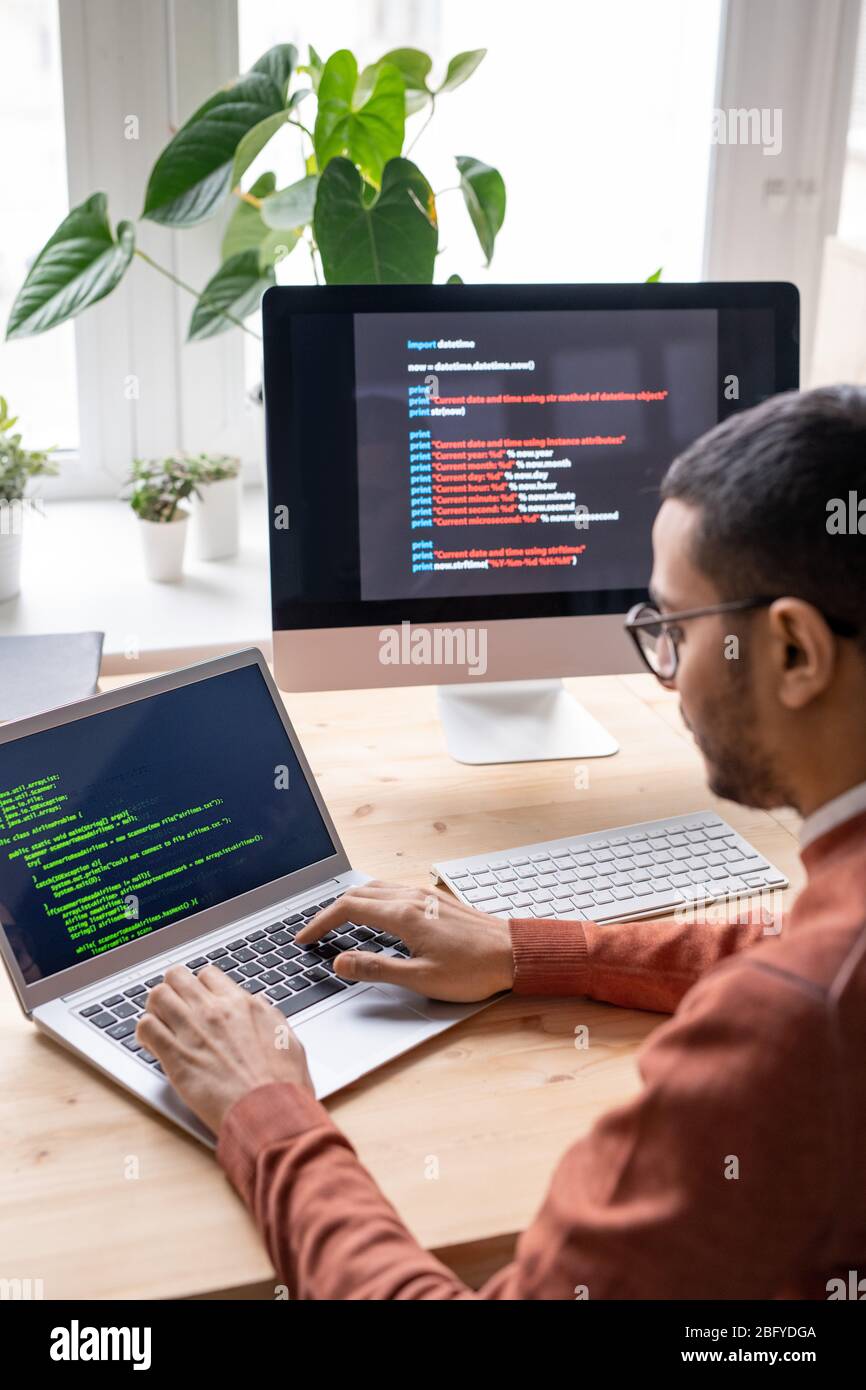 Over shoulder view of young web developer sitting at desk and working ...