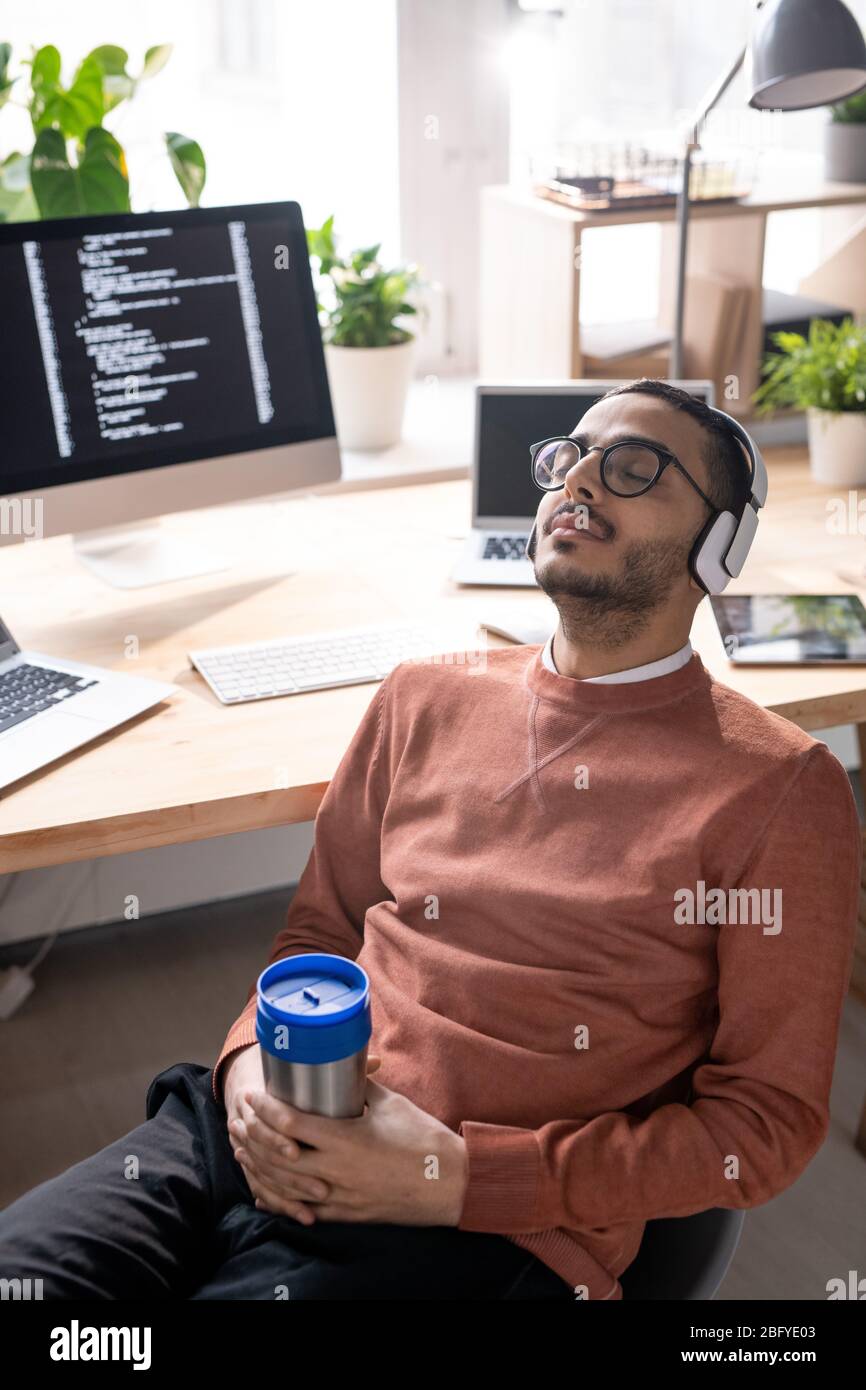 Tired young middle-eastern programmer with stubble sitting with closed ...