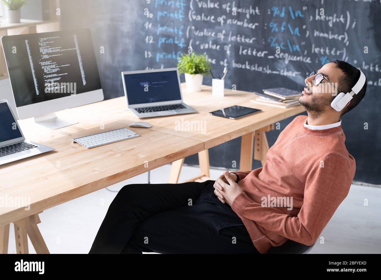Tired young middle-eastern coder in headphones sitting in relaxed pose ...