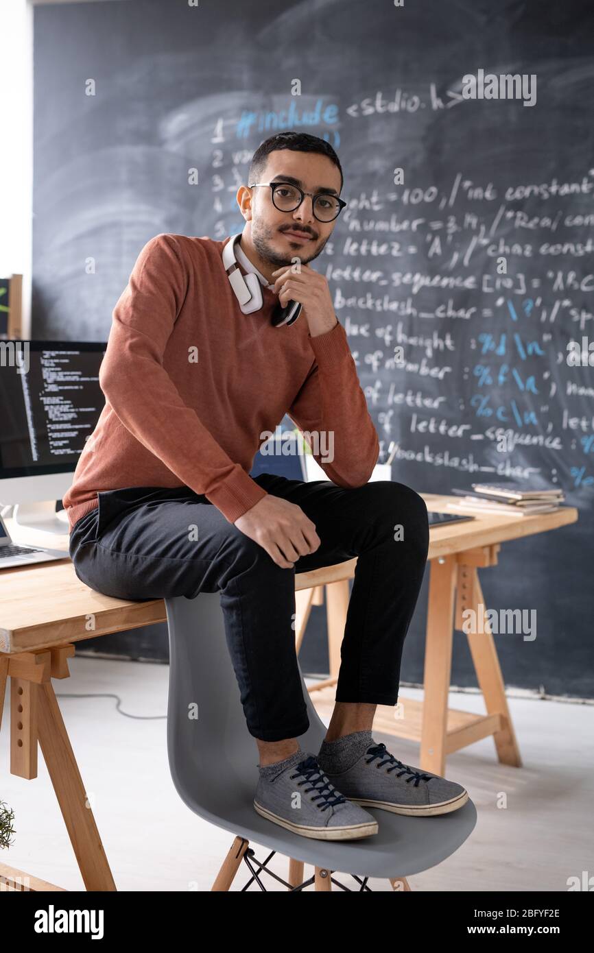 Portrait of serious young Arabian IT engineer sitting on table with ...