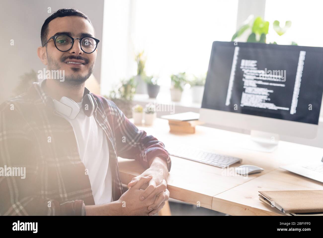 Portrait of positive young middle-eastern coder in glasses sitting with ...