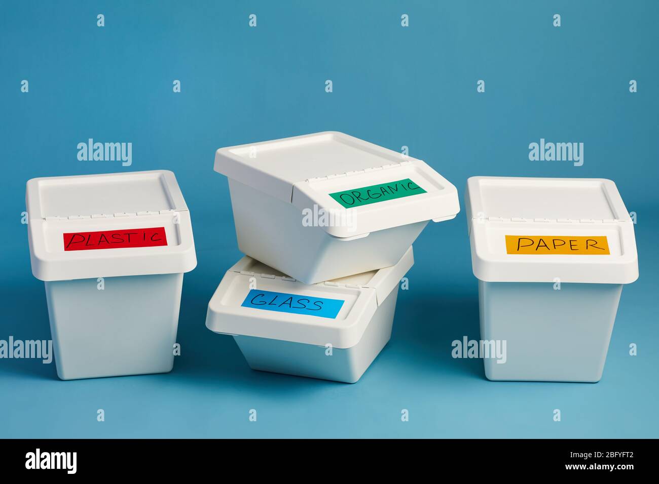 Labeled trash bins for plastic and paper waste in row against blue ...
