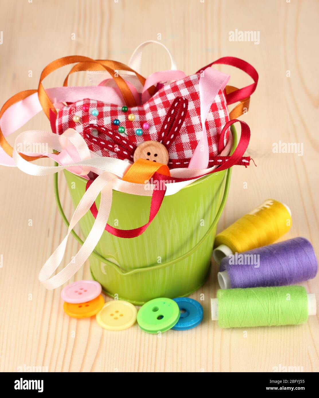 Color bucket with multicolor ribbons and thread on wooden background ...