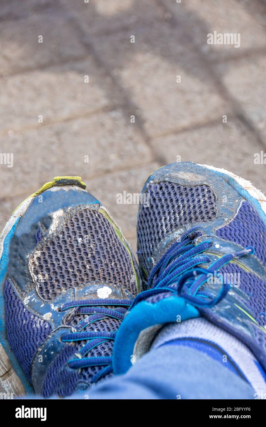 Crossed legs with feet in old trainers isolated on a paved surface ...