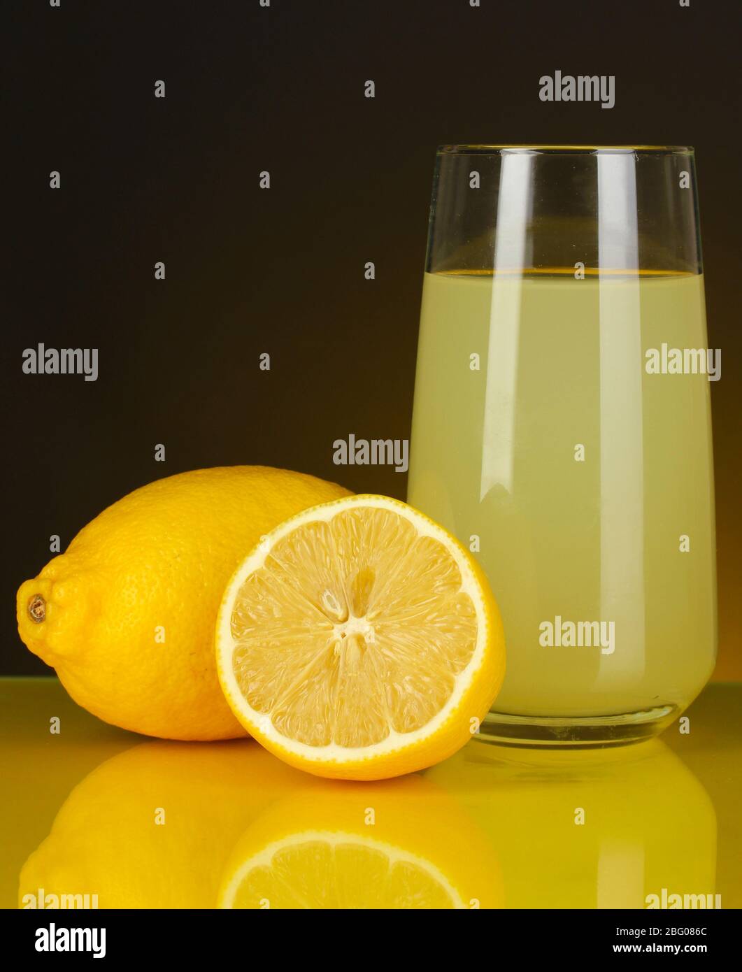 Delicious lemon juice in glass and lemons next to it on dark orange ...