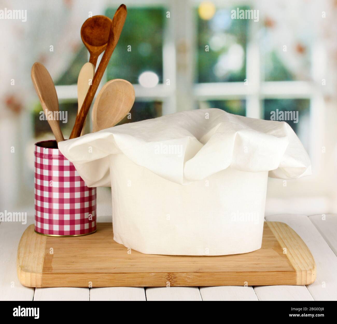 Chef's hat with spoons on board on wooden table on window background ...