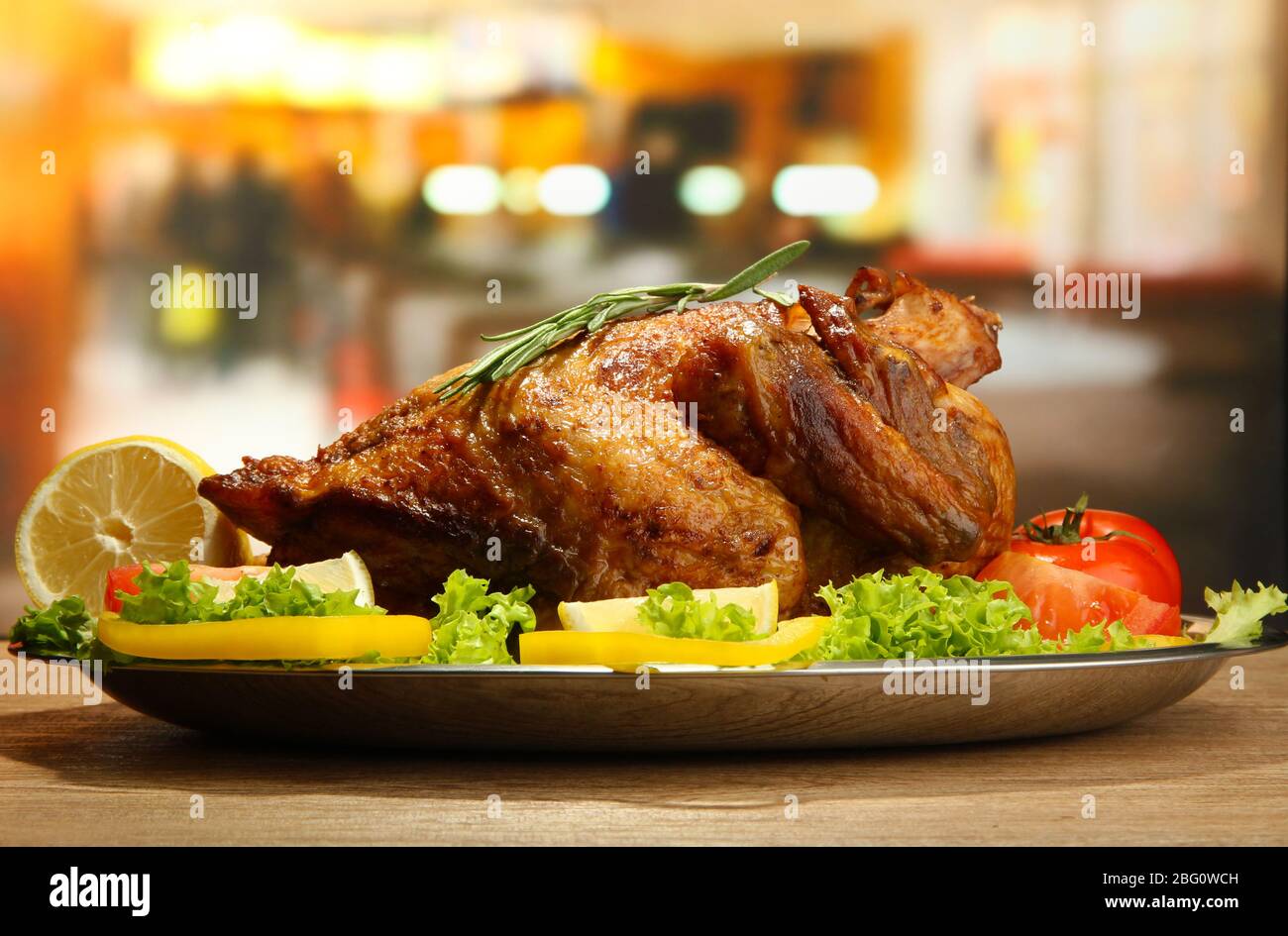 Whole roasted chicken with vegetables on plate, on wooden table in cafe ...