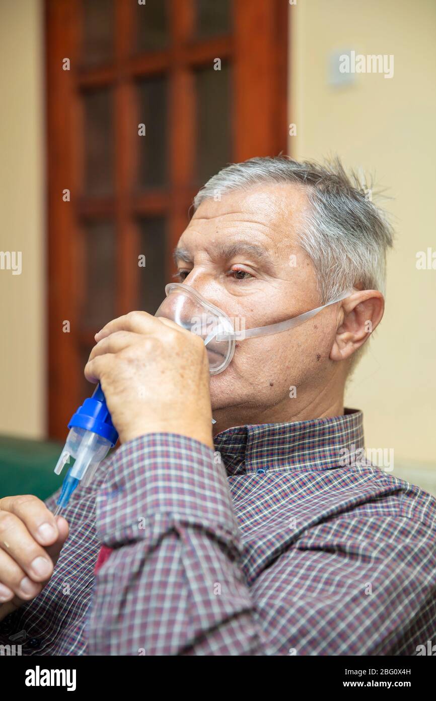 Senior man using medical equipment for inhalation with respiratory mask ...