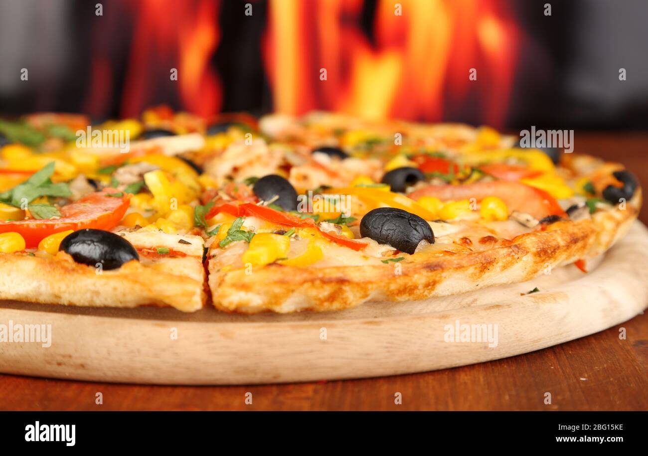 Delicious pizza close-up on wooden table on fire background Stock Photo ...