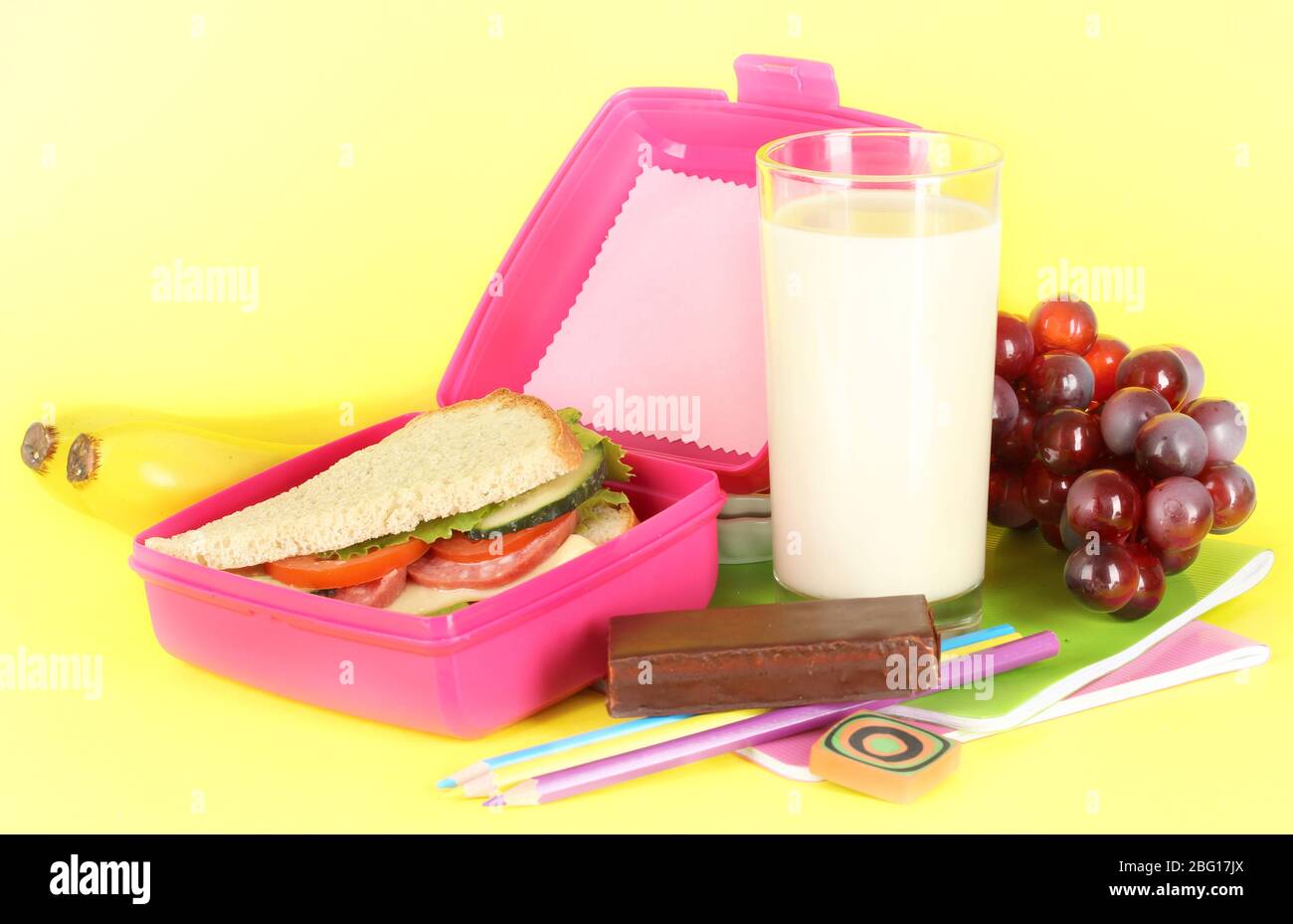 Lunch box with sandwich,grape,milk and stationery on yellow background ...