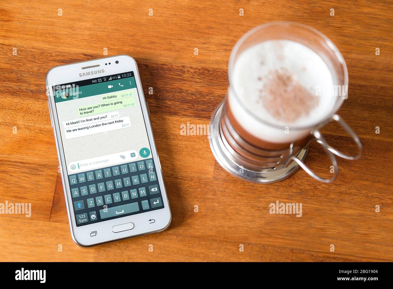 Cell phone over a wood table near a coffee cup. A chat of whatsapp ...