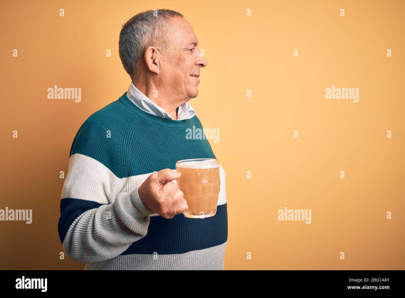 Senior handsome man drinking jar of beer standing over isolated yellow ...