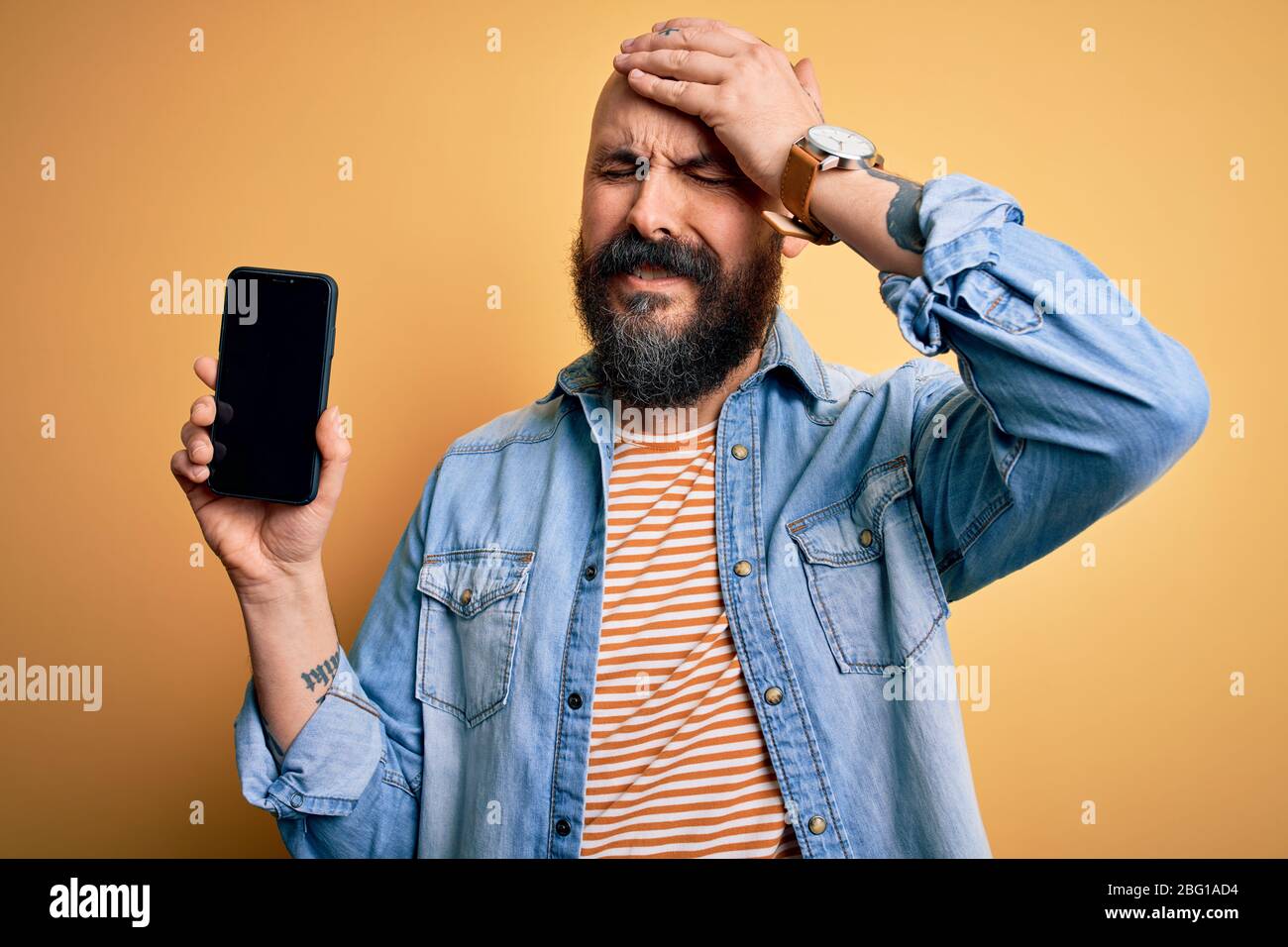 Handsome bald man with beard holding smartphone showing screen over ...