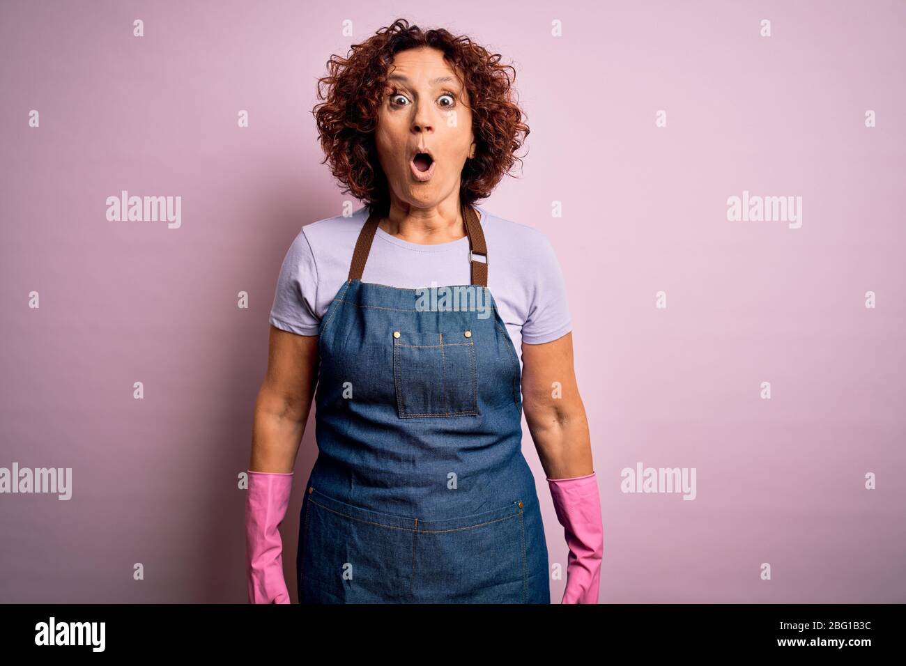 Middle age curly hair woman cleaning doing housework wearing apron and ...