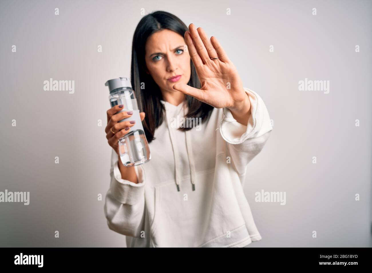Young brunette sporty woman with blue eyes holding water bottle over ...
