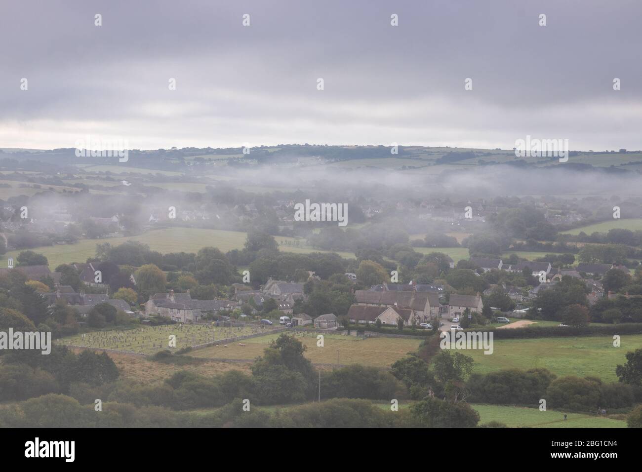 A typical old English village in a valley with mist creeping in over ...