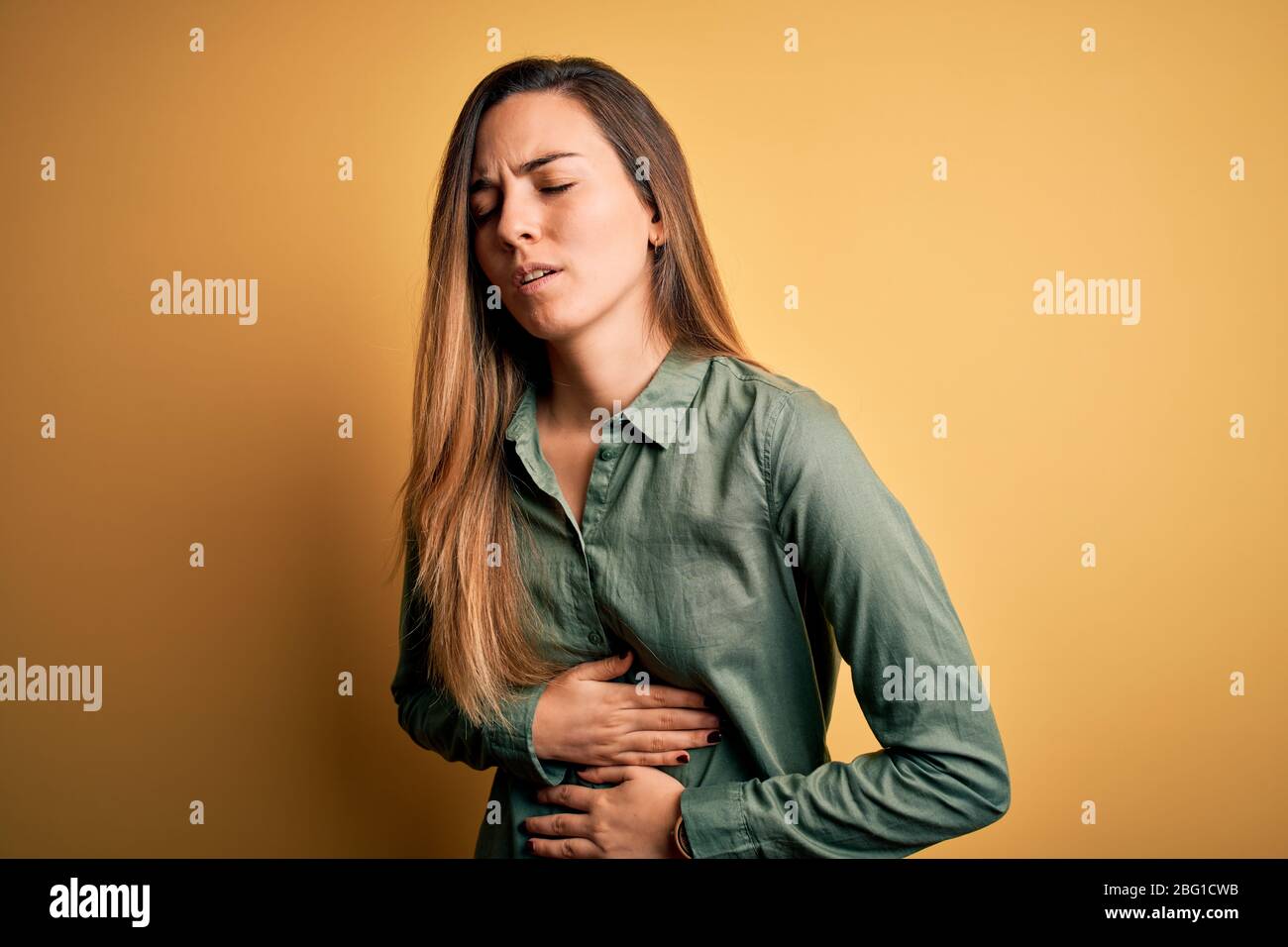Young beautiful blonde woman with blue eyes wearing green shirt over ...