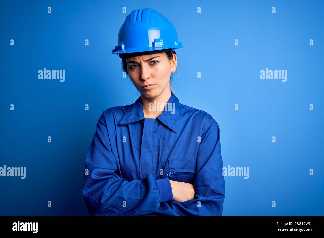 Young beautiful worker woman with blue eyes wearing security helmet and ...