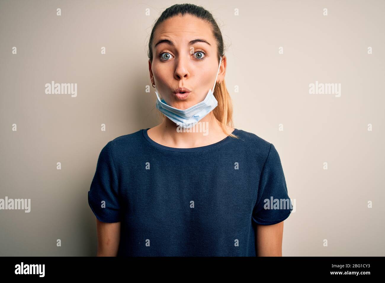 Beautiful blonde woman with blue eyes wearing medical mask over white ...