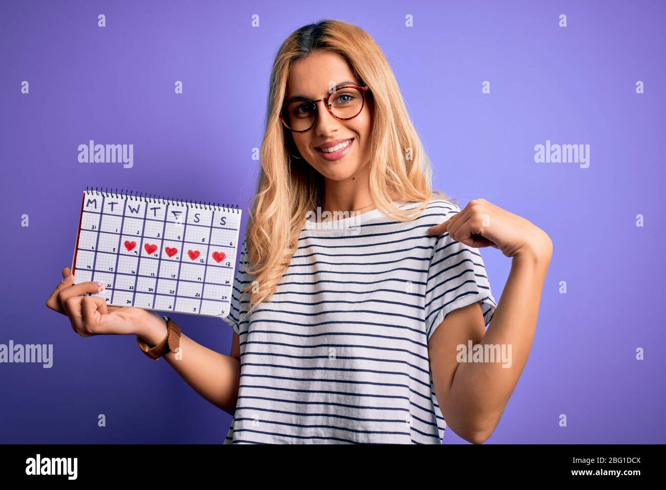 Young beautiful blonde woman holding period calendar to control ...