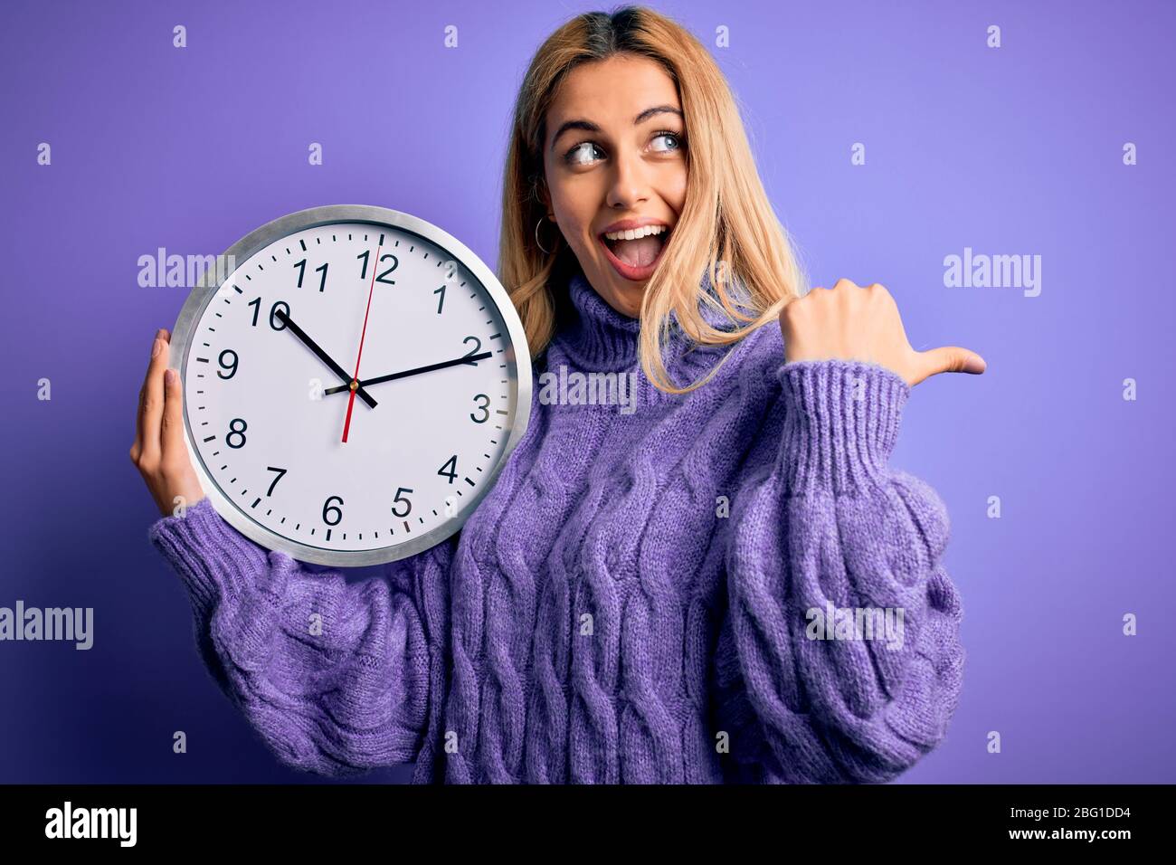 Young beautiful blonde woman doing countdown holding big clock over ...