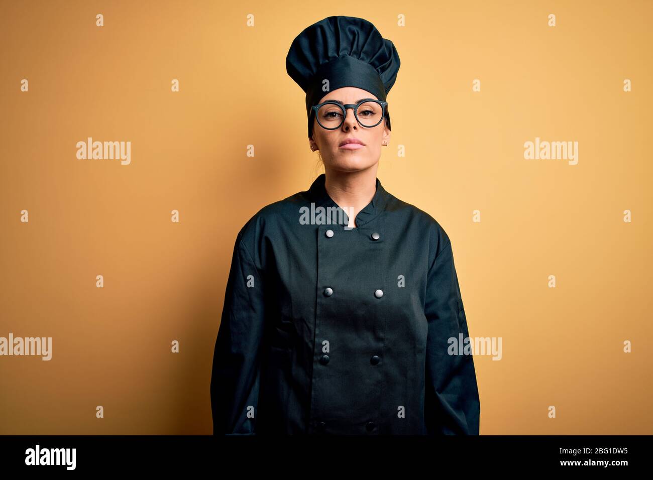 Young beautiful brunette chef woman wearing cooker uniform and hat over ...