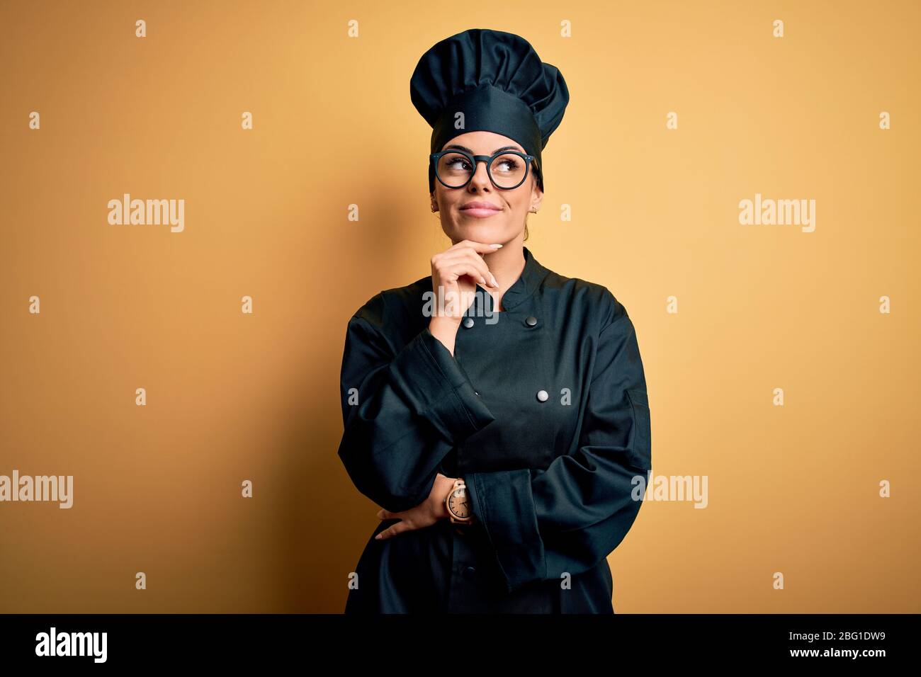 Young beautiful brunette chef woman wearing cooker uniform and hat over ...