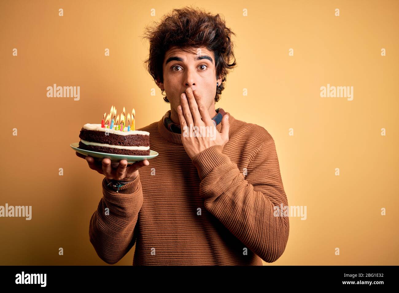 Young handsome man holding birthday cake standing over isolated yellow ...