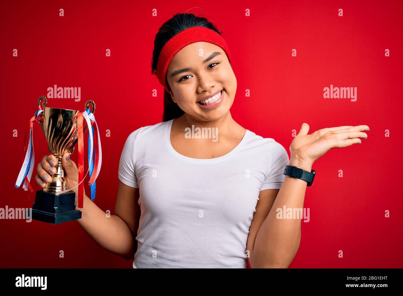 Young champion asian girl winning trophy cup standing over isolated red ...