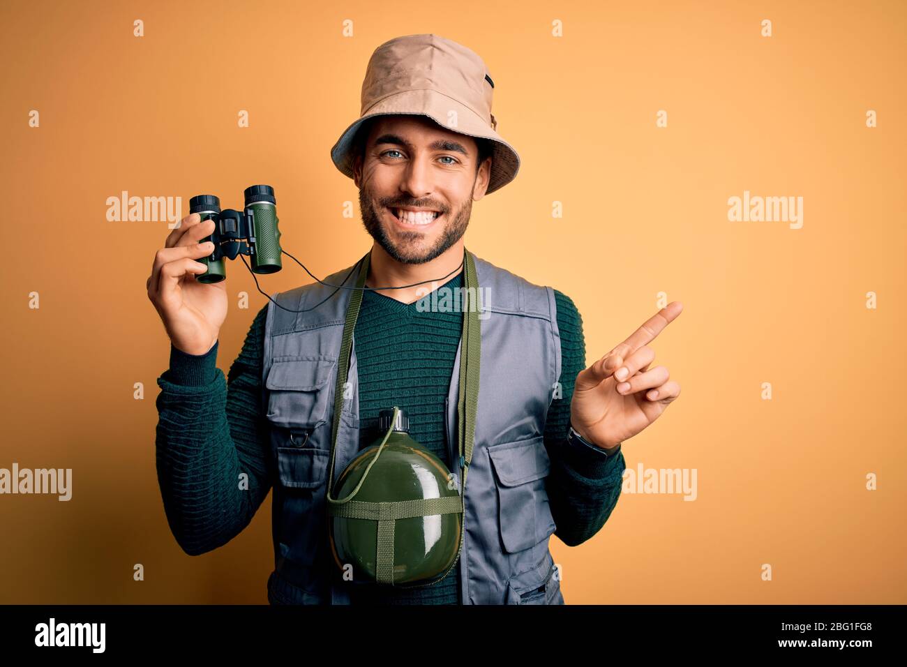 Young handsome tourist man with beard on vacation wearing explorer hat ...