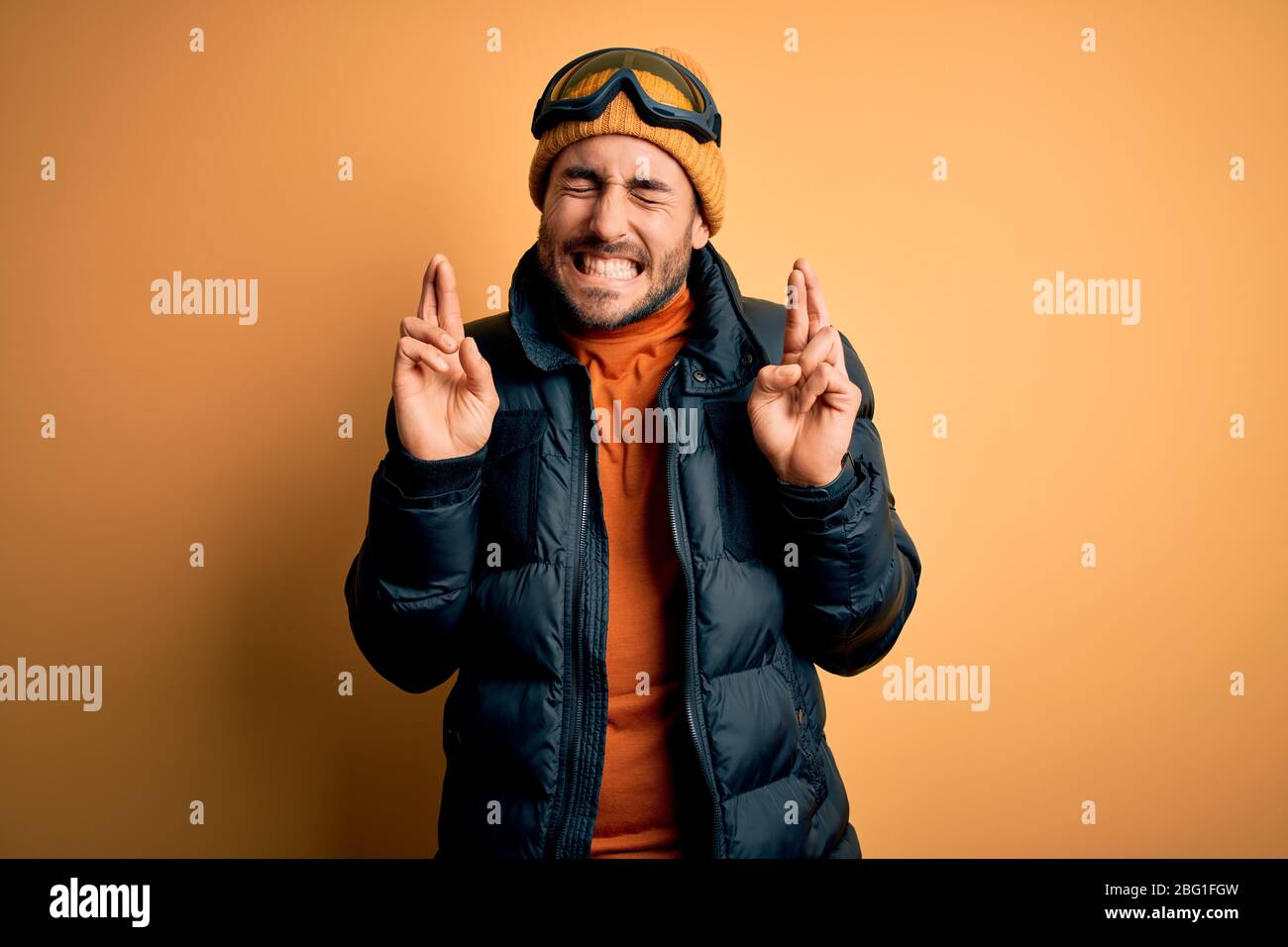 Young handsome skier man with beard wearing snow sportswear and ski ...