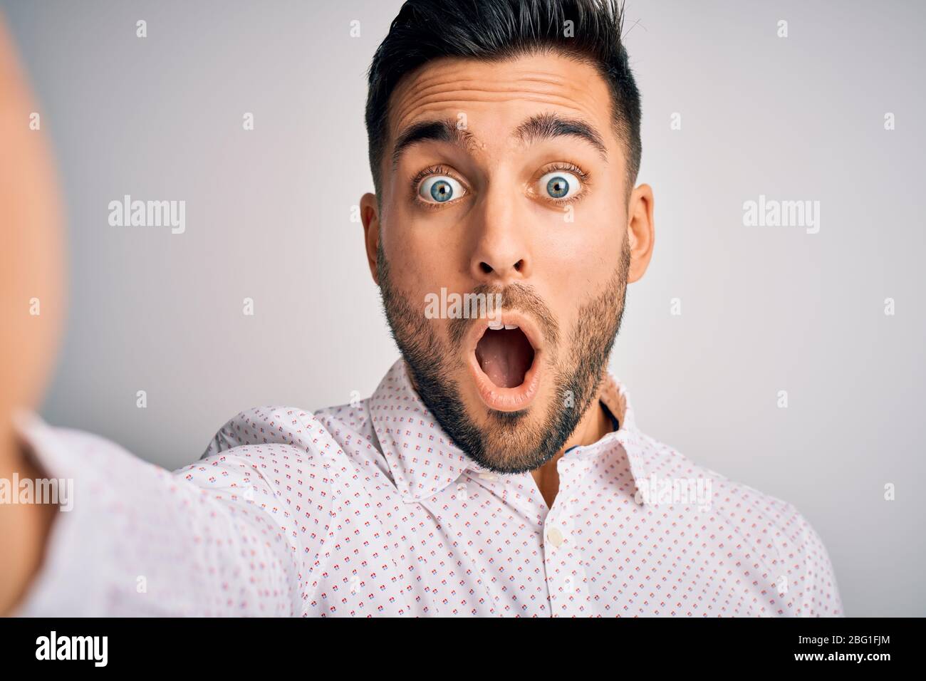 Young handsome man wearing shirt making selfie by the camera over white ...