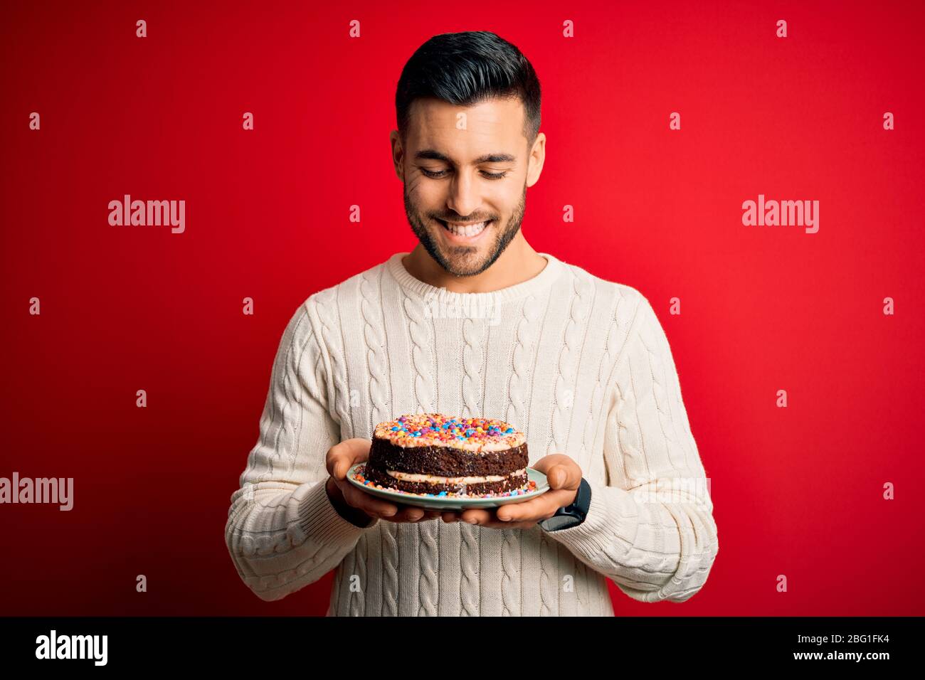Young handsome man holding colorful birthday sweet cake over red ...
