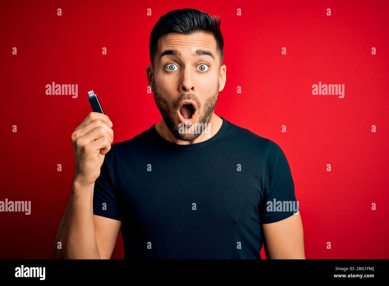 Young man holding USB memory data drive over red isolated background ...
