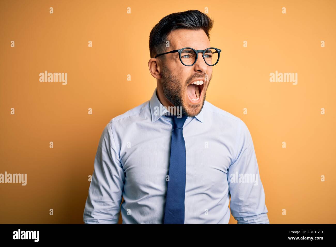 Young handsome businessman wearing tie and glasses standing over yellow ...