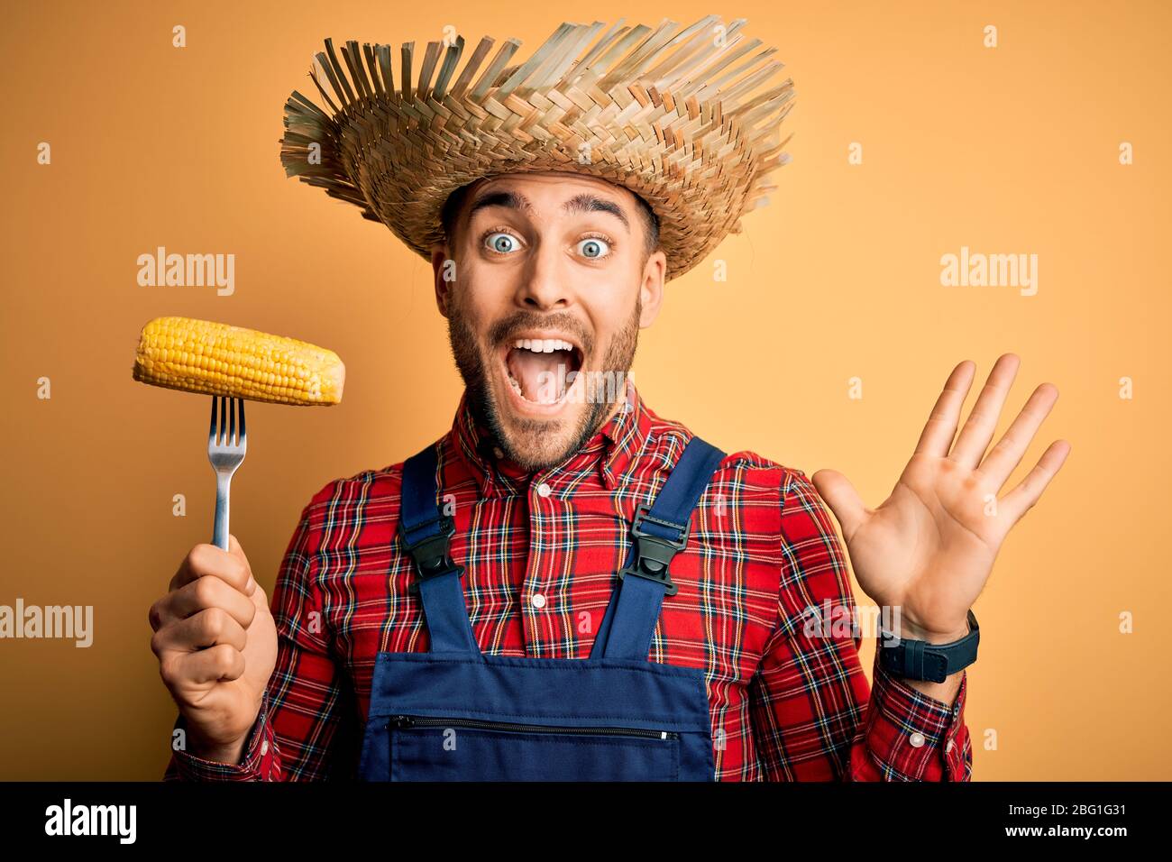 Young rural farmer man holding countryside corn over isolated yellow ...