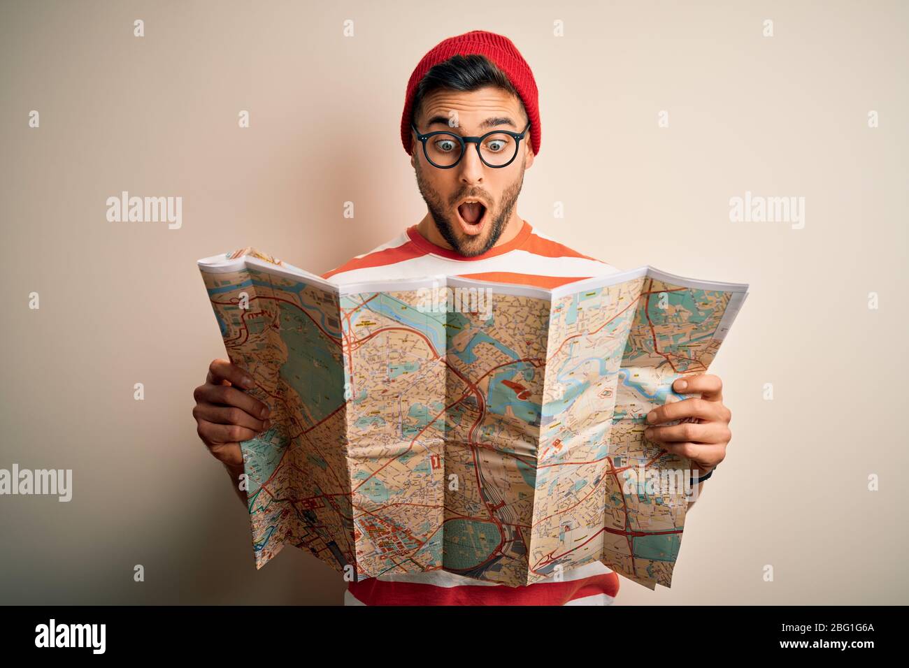 Young handsome tourist man on vacation wearing glasses holding city map ...