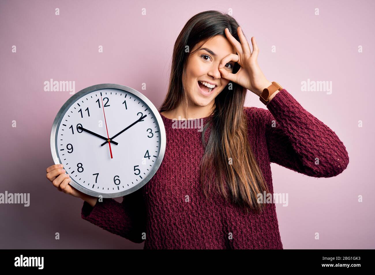 Young beautiful girl doing countdown holding big clock over isolated ...
