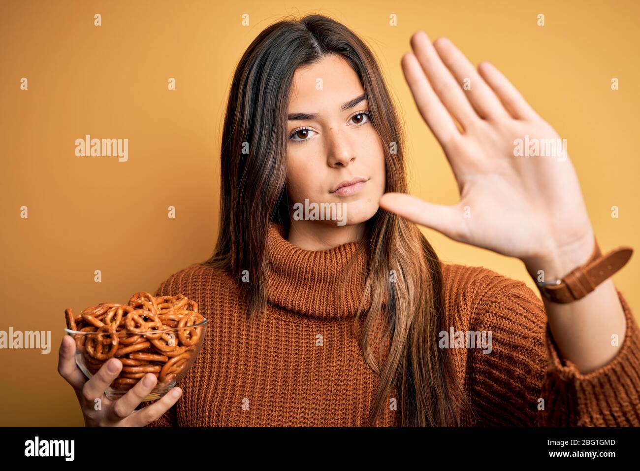 Young beautiful girl eating baked german pretzel standing over isolated ...