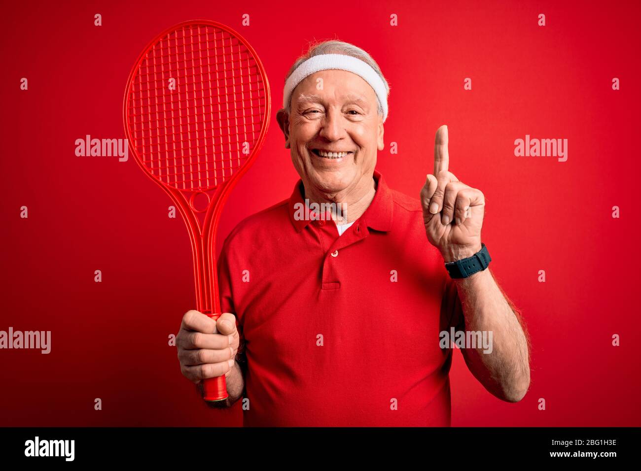 Grey haired senior tennis player man holding racket over red isolated ...