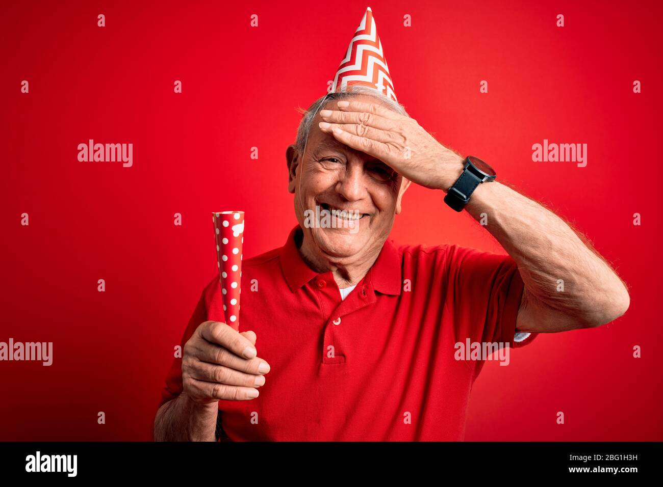 Senior grey haired man wearing birthday hat and holding party trumpet ...