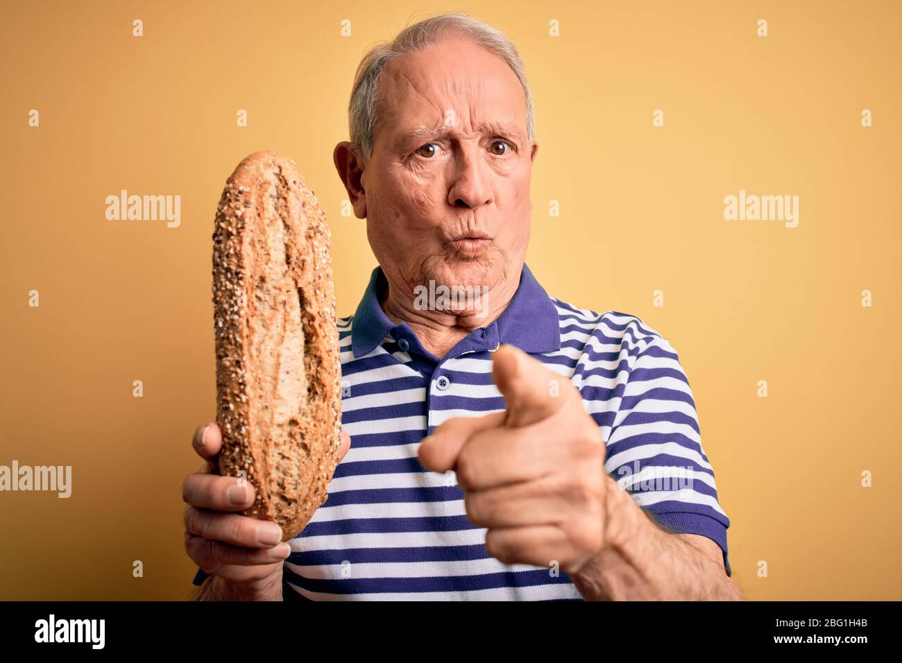 Grey haired senior man holding healthy wholemeal bread over yellow ...