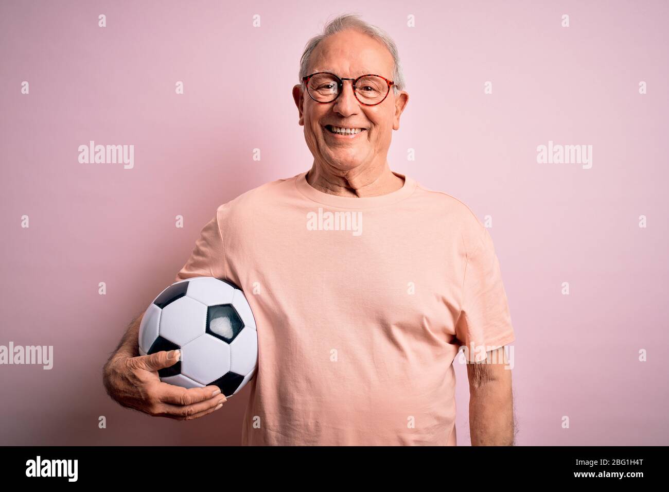Grey haired senior football player man holding soccer ball over pink ...