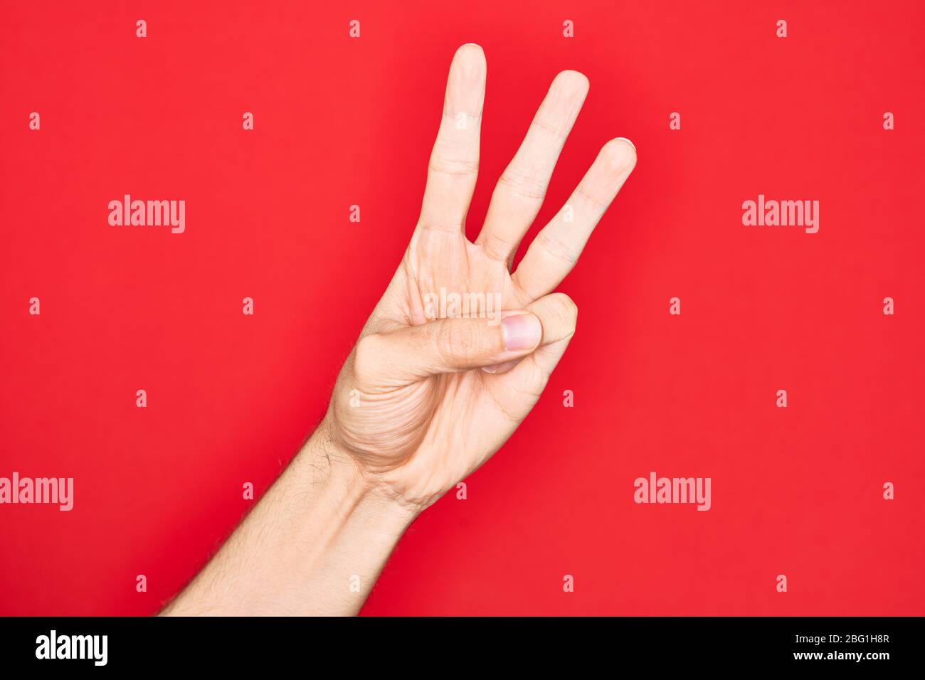 Hand of caucasian young man showing fingers over isolated red background counting number 3 ...