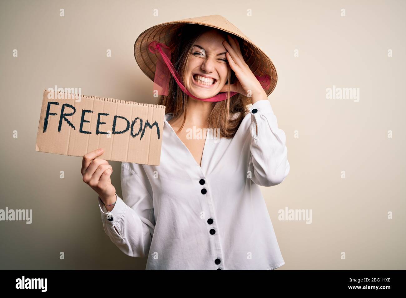 Young redhead woman wearing asian traditional hat holding banner with ...
