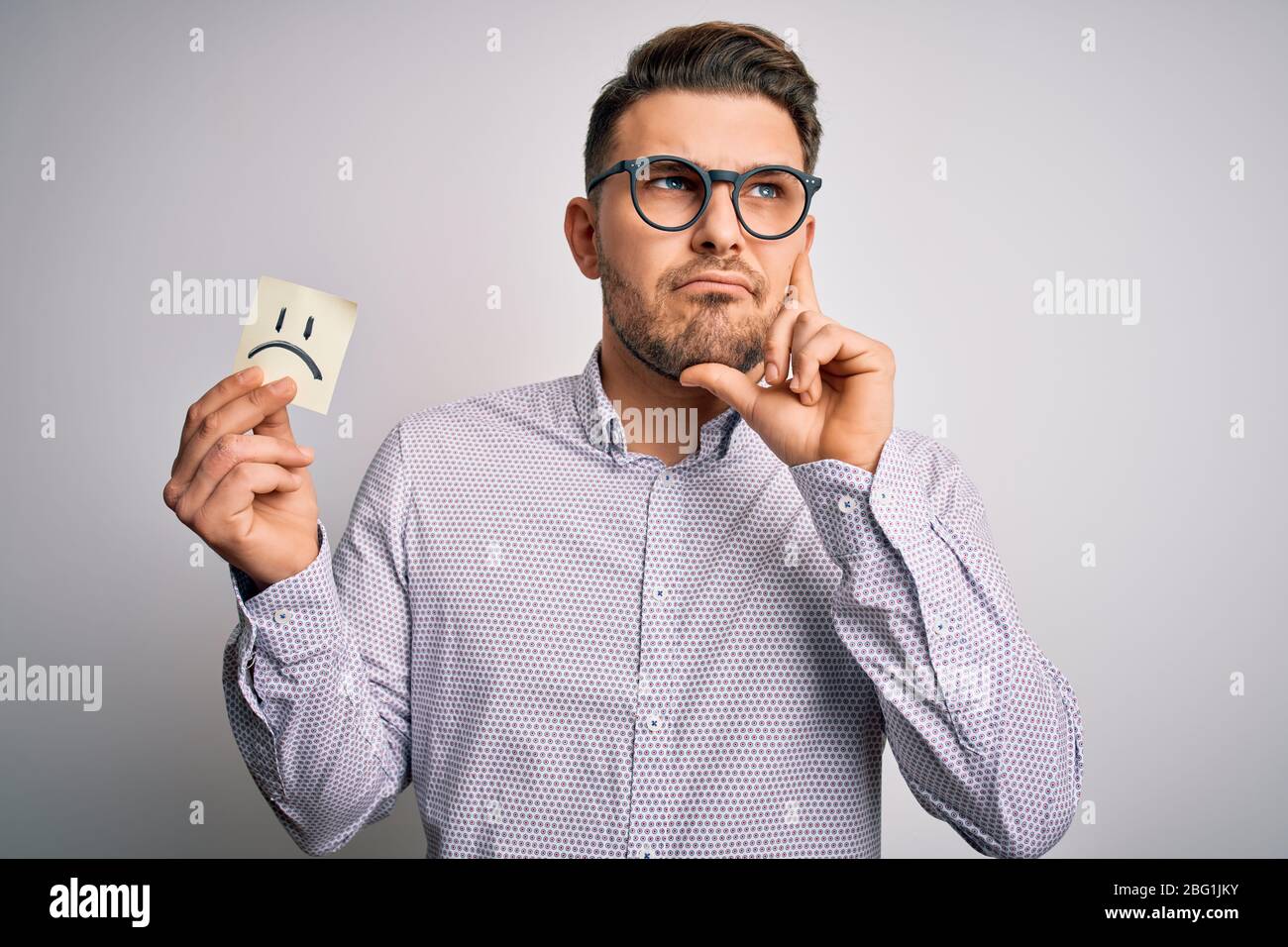 Young business man with blue eyes holding paper note with sad face as ...